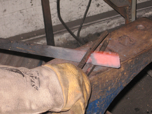 The two parallel arms of a spring fuller are applied to a glowing red ...